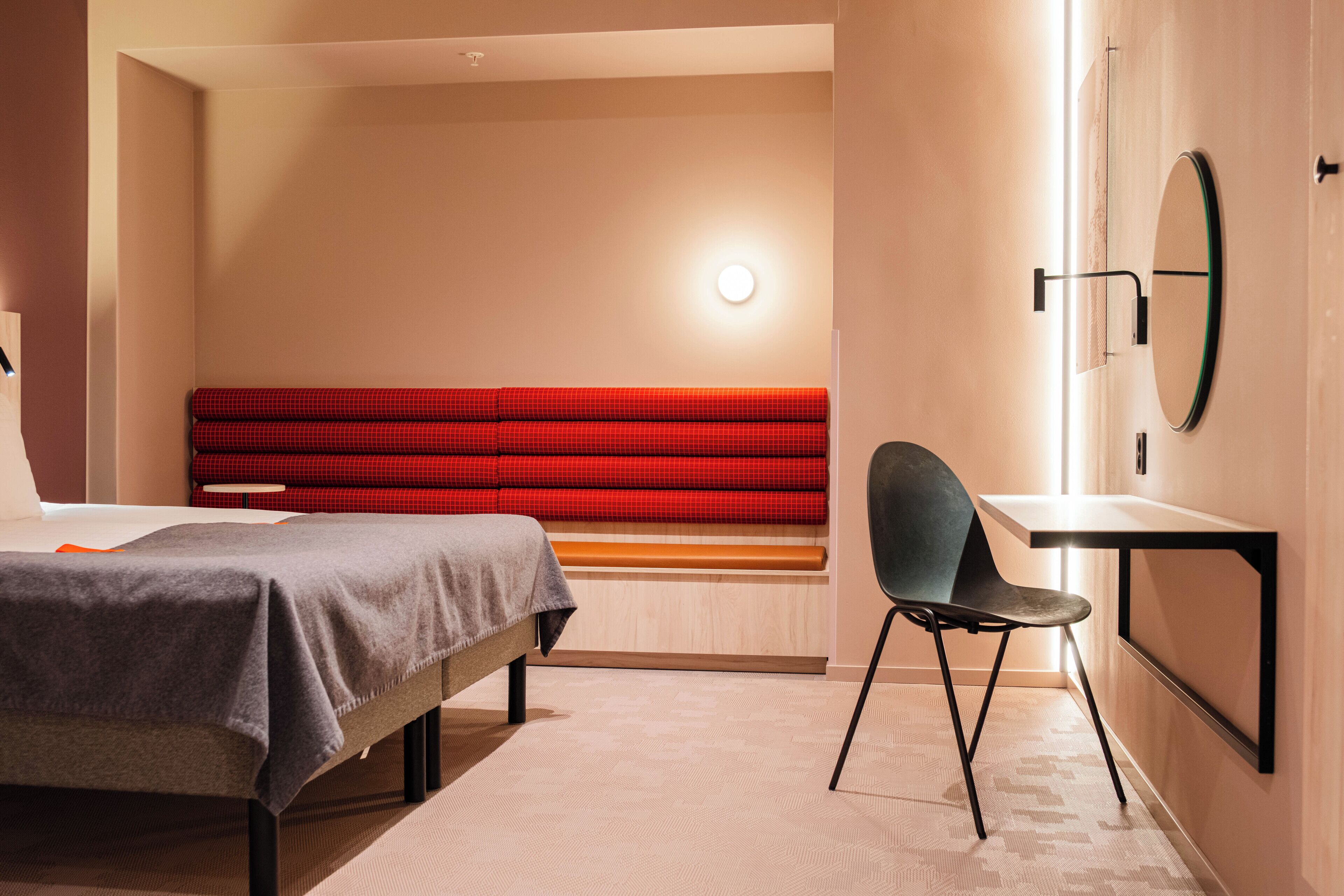Quarto moderno com cama, um banquinho vermelho, escrivaninha e espelho.