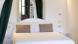 Cama bem arrumada com almofadas brancas e castanhas, uma pequena mesa de cabeceira e um aparelho de luz fixado na parede.