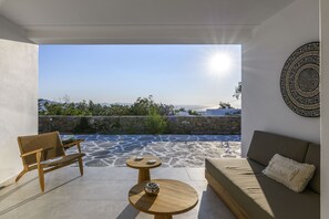Uma área externa moderna com assentos, piso de lajes de pedra, um banco de madeira, uma mesa redonda e um sofá.