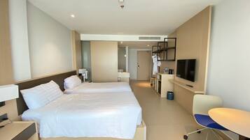 Quarto de hotel com duas camas, uma escrivaninha, uma cadeira, uma televisão e banheiro.