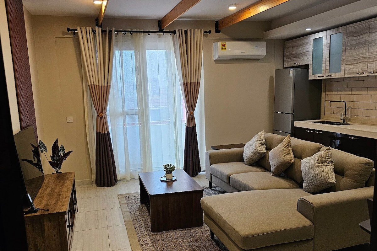 Uma sala de estar moderna com sofá, mesa de centro e cozinha, incluindo geladeira e armários.