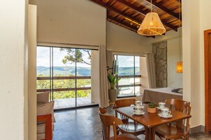 Uma área de jantar com uma mesa posta para dois, grandes janelas com vista para as montanhas e um lustre.