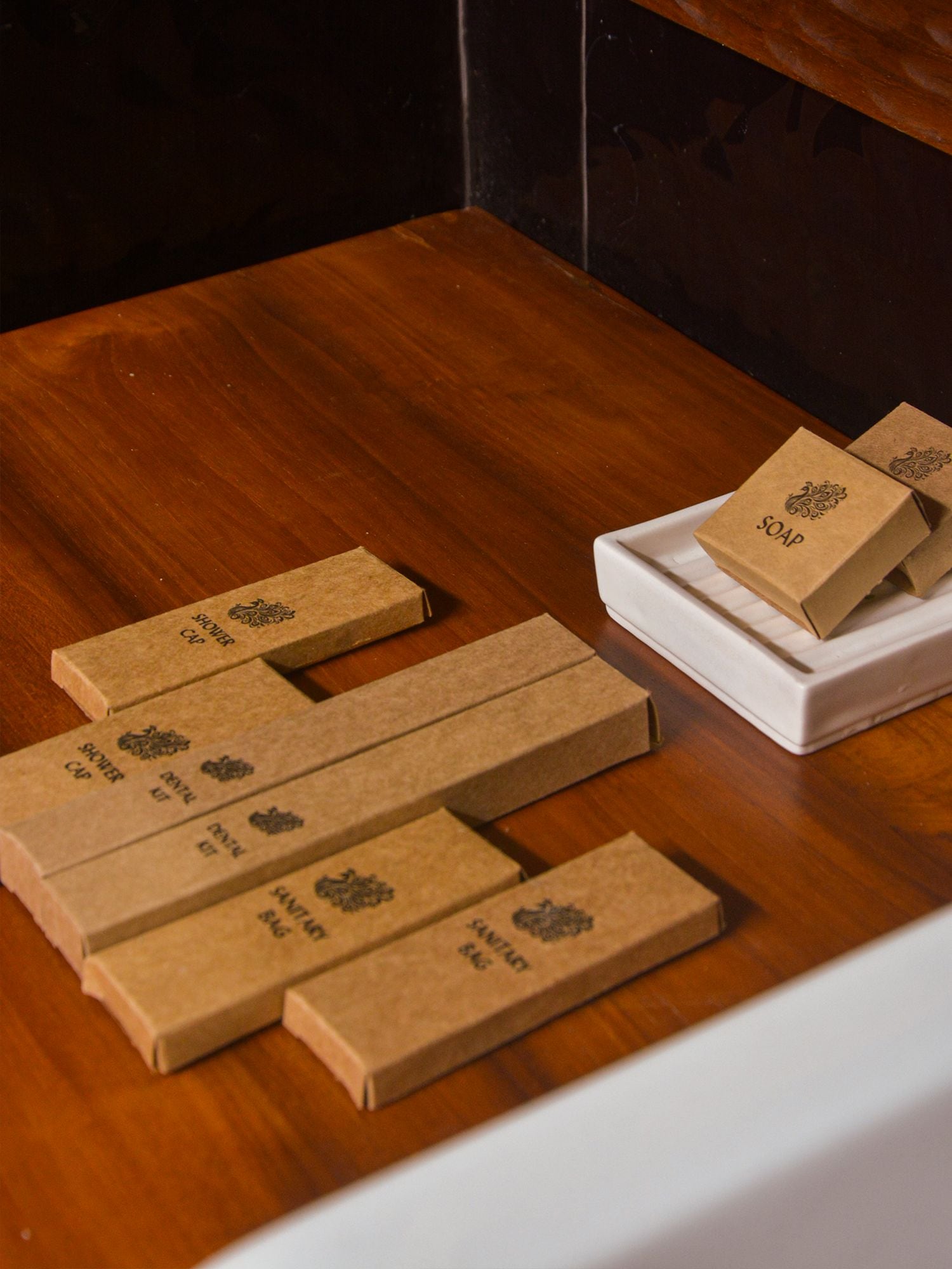 Uma mesa de madeira com várias caixas de papelão etiquetadas com diferentes comodidades como 'SHOWER CAP', 'BATH CAP' e 'SOAP'.