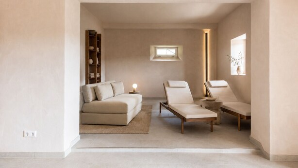 Uma sala de estar minimalista com um sofá, duas poltronas, uma mesa lateral, um abajur, uma estante de livros e uma janela pequena.
