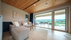 Uma sala de estar moderna com um sofá, uma mesa de centro e vista para uma varanda com mobiliário de exterior.