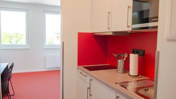 Cozinha moderna com armários brancos, parede de destaque vermelha, micro-ondas embutido e janela com vista para o verde.