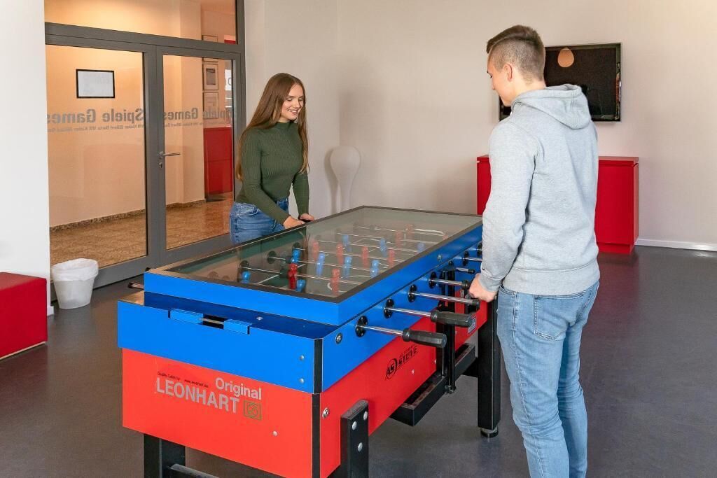 Uma mesa de futebol em uma sala com divisória de vidro e esquema de cores vermelho e azul.
