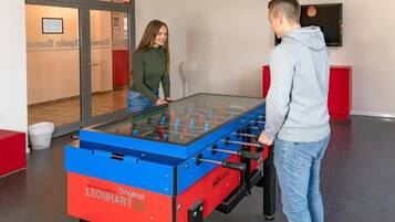 Uma mesa de futebol em uma sala com divisória de vidro e esquema de cores vermelho e azul.