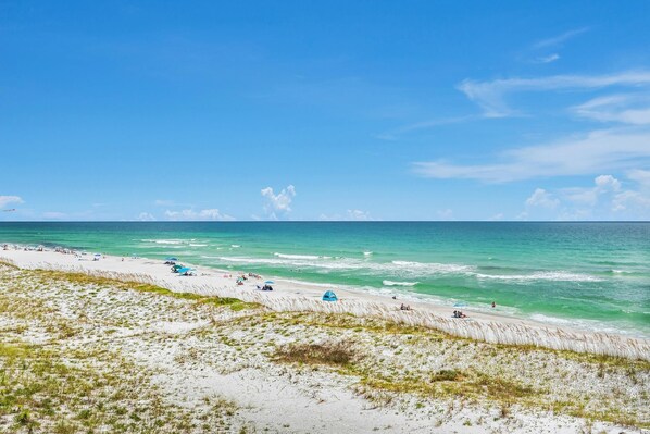 Uma praia com areia branca, águas turquesa cristalinas e algumas barracas.