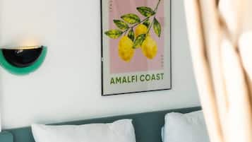 Quarto de hotel com uma cama, duas almofadas, uma mesinha de cabeceira, uma luminária na parede e um quadro com limões.