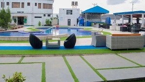 Área de piscina com espreguiçadeiras e um espaço de estar coberto, cercada por edifícios.