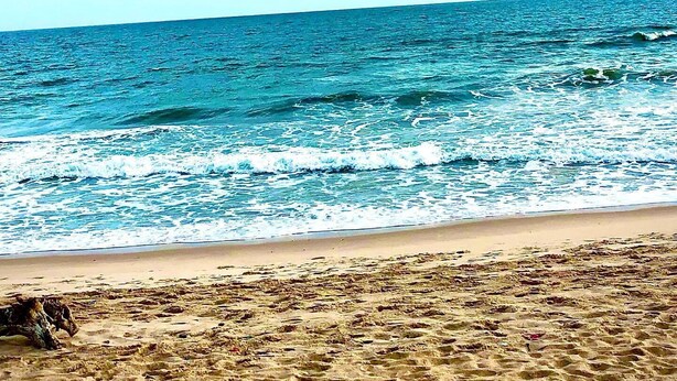 Uma praia com ondas, uma faixa de areia e um céu nublado.