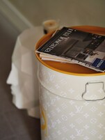 Um recipiente branco com padrão Louis Vuitton, contendo revistas e uma xícara de café.