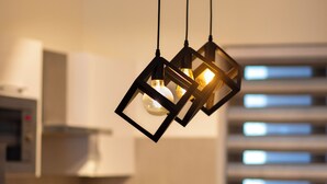 Cozinha com luminárias pendentes, micro-ondas e janela com persianas.
