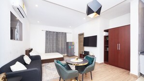 Quarto de hotel moderno com sofá, duas cadeiras, uma mesinha redonda, televisão, guarda-roupa e cama.