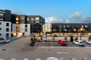 Um complexo de apartamentos moderno, com vários edifícios, uma área de estacionamento e alguns carros.