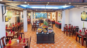 Restaurante com área central de buffet, várias mesas de jantar e luminárias decorativas pendentes.