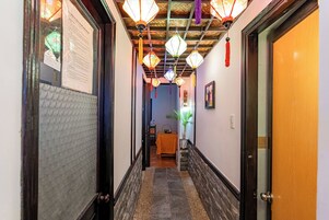 Um corredor com piso de pedra, uma porta de madeira à direita e uma mesa com toalha amarela ao longe.
