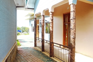 Uma galeria coberta com piso de azulejos, guarda-corpo de metal e um edifício com fachada bege e molduras de janela de madeira.