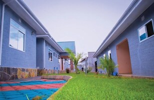 Um edifício moderno com fachada azul, um pátio pavimentado com azulejos coloridos e um gramado bem cuidado.
