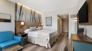 Quarto de hotel com cama, sofá azul, escrivaninha com televisão de tela plana e obra de arte na parede.