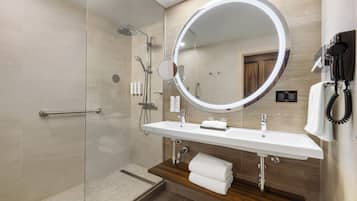 Casa de banho moderna com cabine de duche em vidro, toucador com um espelho grande e secador de cabelo fixado na parede.