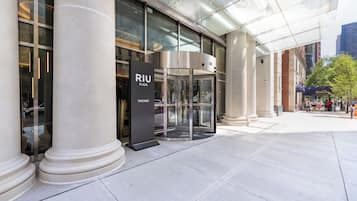 Entrada de um edifício moderno com porta giratória, colunas imponentes e fachada de vidro.