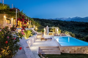 Área à beira da piscina com parede de pedra, escadas para um deck e vista para montanhas ao fundo.