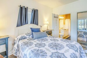 Quarto com cama grande, mesa de cabeceira, abajur, espelho e banheiro visível por uma porta aberta.