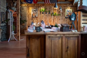 Interior rústico com paredes de madeira, um balcão central de madeira, luminárias pendentes e várias decorações, incluindo uma bandeira e um quadro.