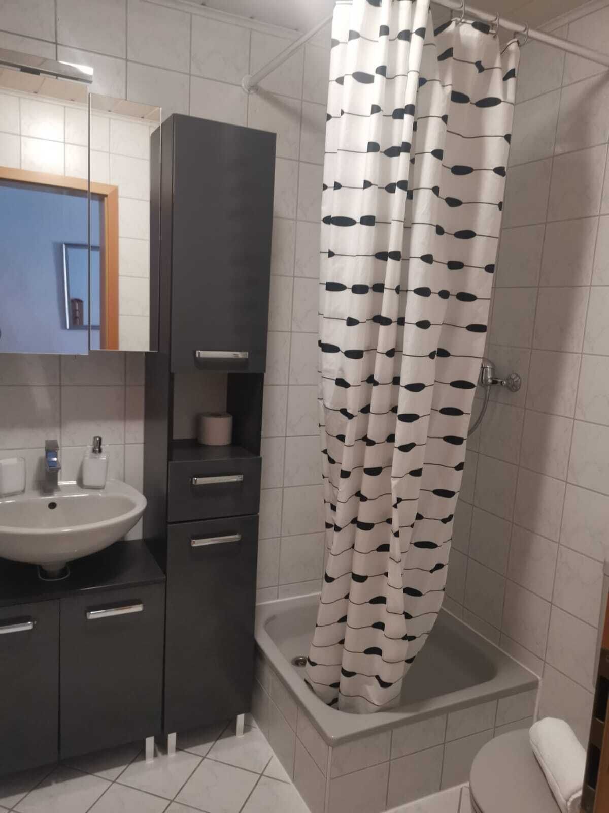 Um banheiro com pia, espelho, armários escuros, chuveiro com cortina estampada e vaso sanitário.
