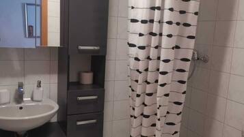 Um banheiro com pia, espelho, armários escuros, chuveiro com cortina estampada e vaso sanitário.