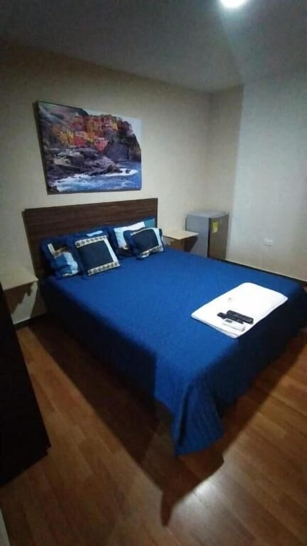 Quarto com cama, mesa de cabeceira, um quadro e escrivaninha.