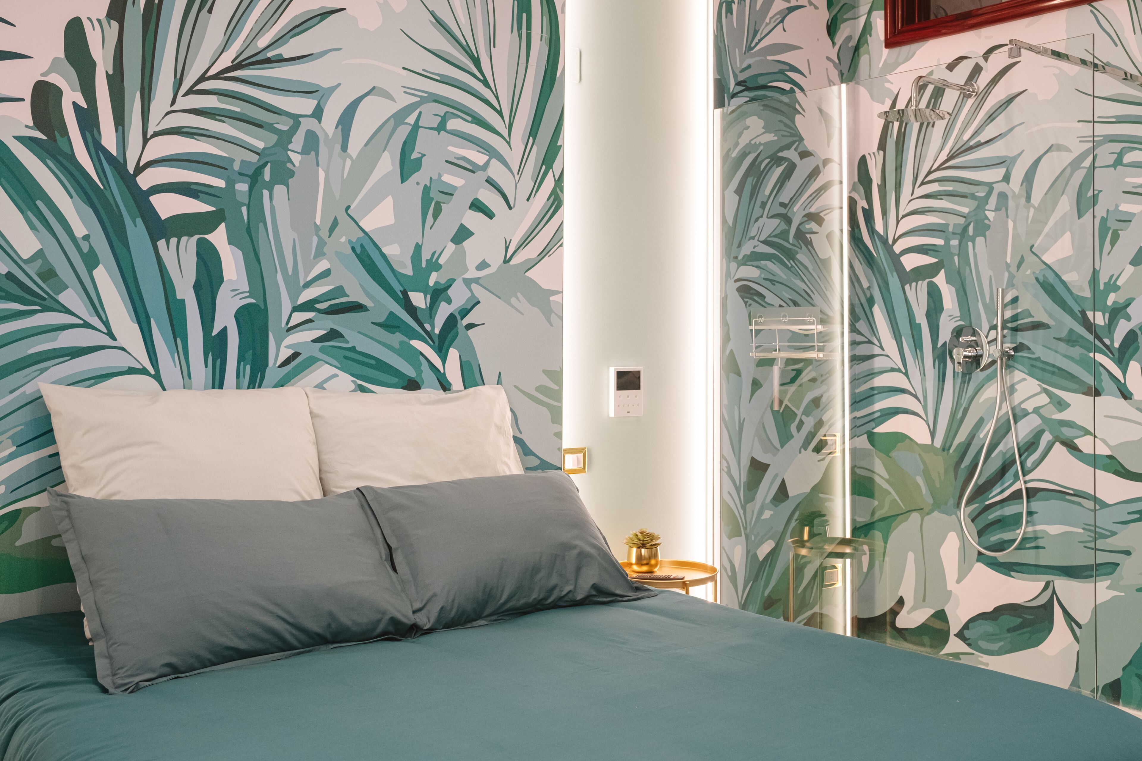 Quarto com cama, almofadas, mesa de cabeceira e área de duche com porta de vidro.