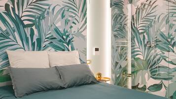 Quarto com cama, almofadas, mesa de cabeceira e área de duche com porta de vidro.