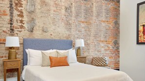 Cama com cabeceira azul, roupa de cama branca e duas mesas de cabeceira com abajures.