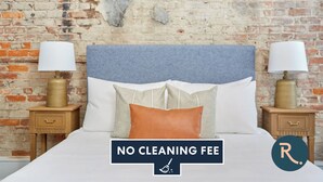 Quarto de hotel com parede de tijolos, uma cama com roupa de cama branca e duas mesas de cabeceira com abajures.