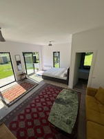 Quarto moderno com cama, poltrona amarela e uma janela grande.