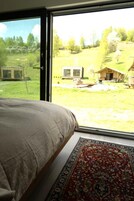 Quarto com uma cama grande, vista para uma paisagem verde através de uma porta deslizante e um tapete estampado no chão.