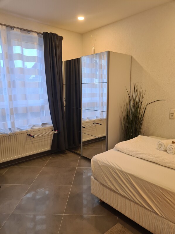 Quarto de hotel com cama, radiador, espelho e janela com cortinas.