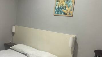 Quarto de hotel com uma cama, mesa de cabeceira, ar condicionado fixado na parede e uma fotografia emoldurada de uma estrela-do-mar.