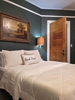 Um quarto com uma cama, um quadro, um abajur e uma porta de madeira.