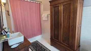 Casa de banho com armário de madeira, pia branca, cortina de chuveiro rosa e tapete estampado.