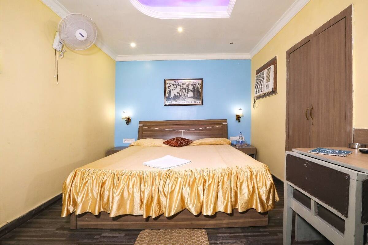 Quarto de hotel com uma cama, uma escrivaninha, um ventilador, ar condicionado fixado na parede e um quadro emoldurado.