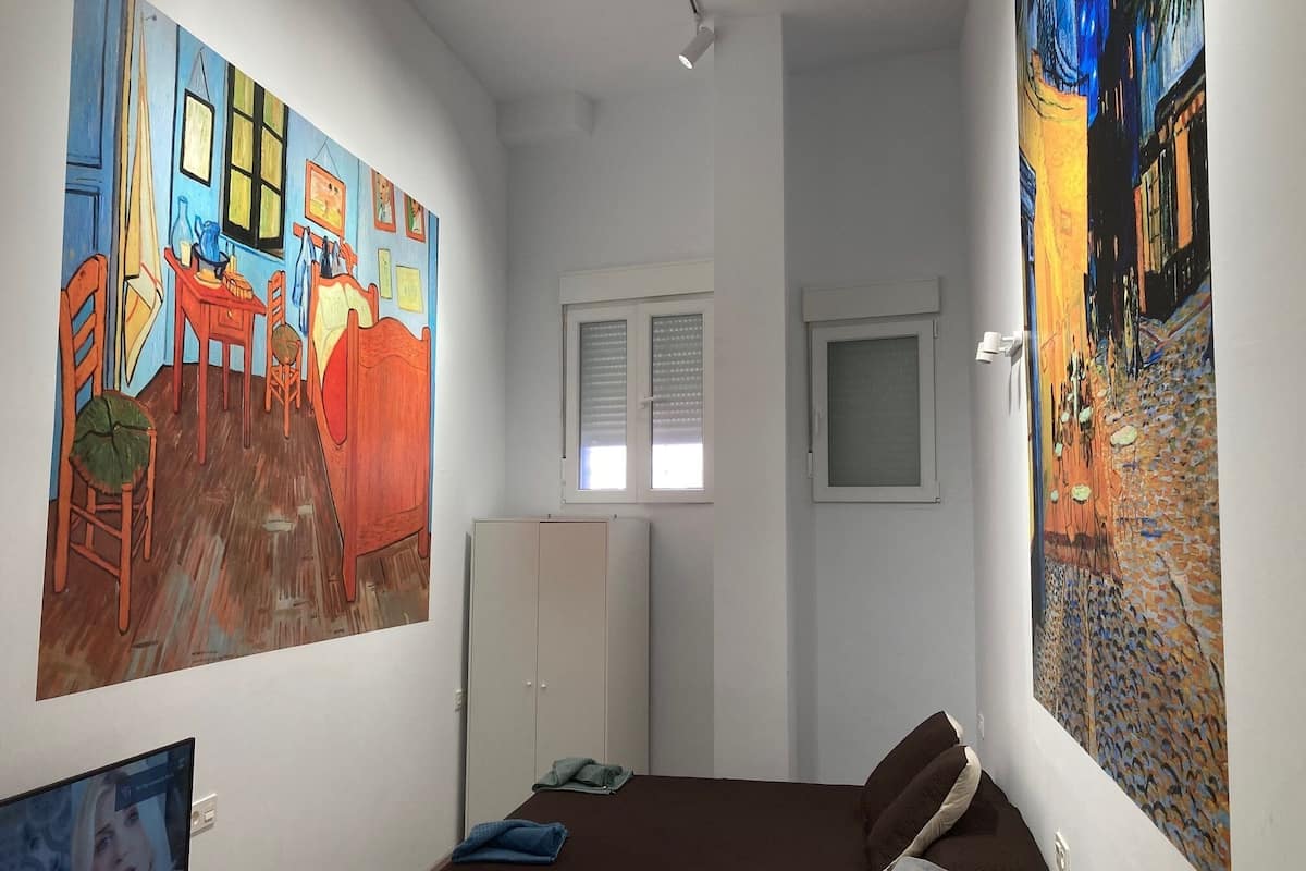 Um quarto com uma cama, uma janela e duas pinturas nas paredes.