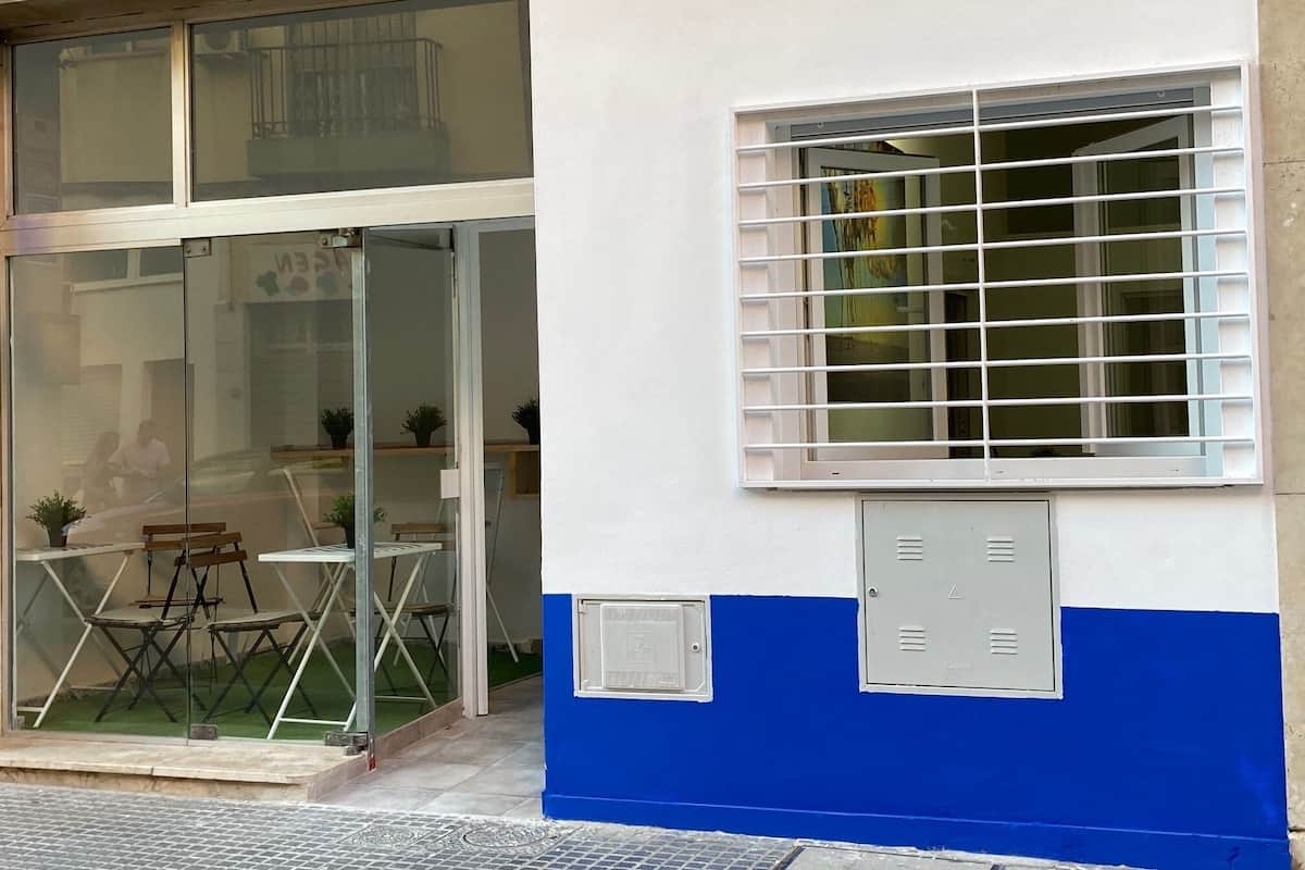 Um edifício com entrada por porta de vidro, janela com persianas horizontais e fachada azul e branca.