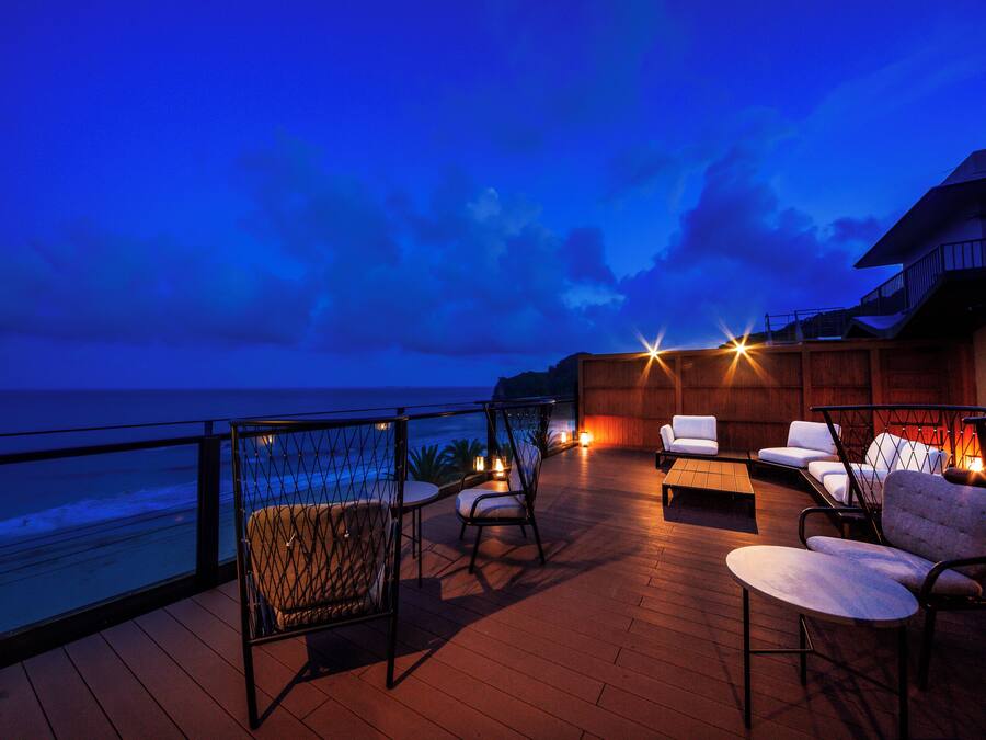 Um terraço com área de estar ao ar livre, vista para o oceano e um edifício com varanda.