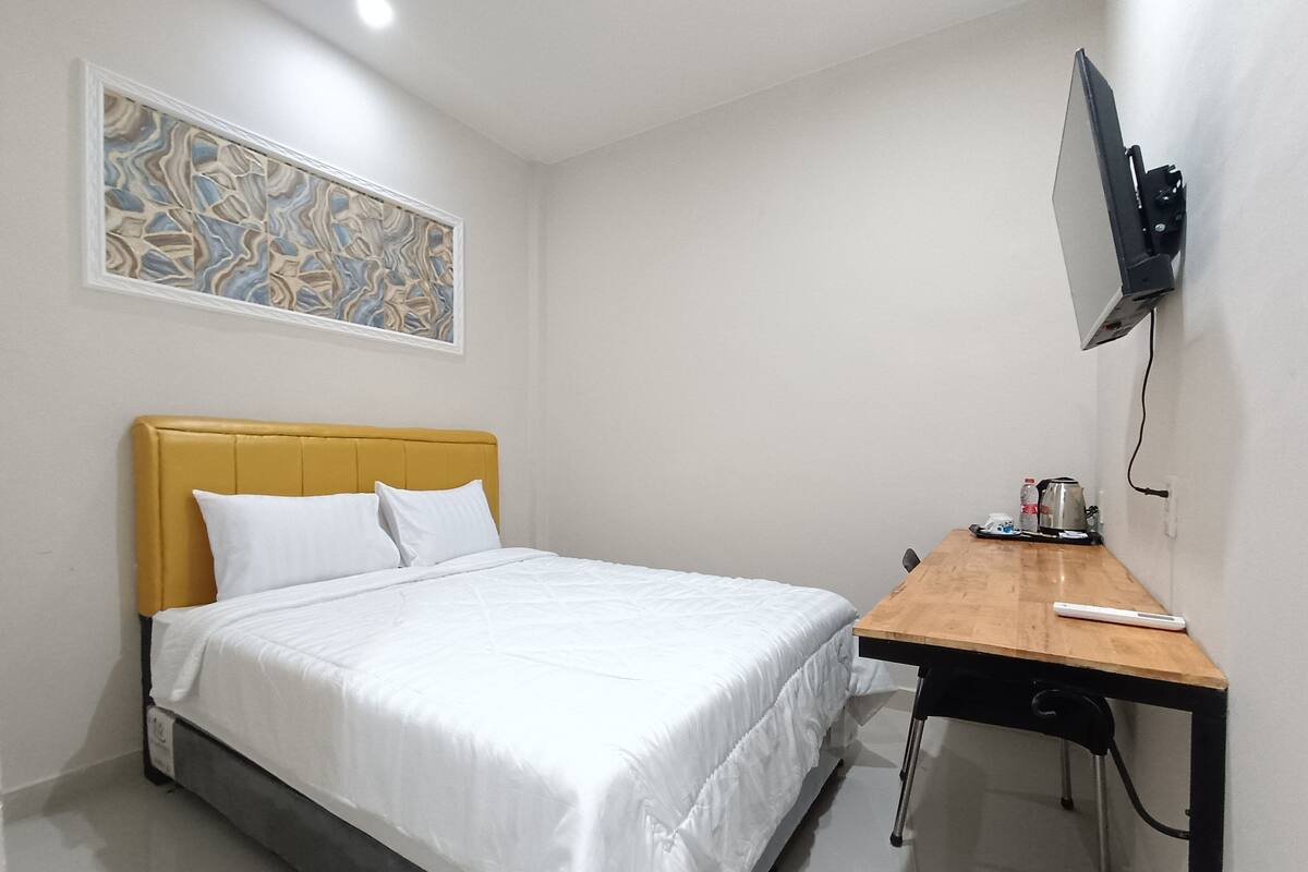 Quarto com cama, escrivaninha, televisão e um quadro na parede.