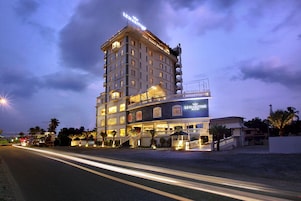 Um hotel com vários andares, um letreiro chamativo, várias varandas e uma entrada bem iluminada.