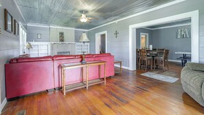 Uma sala ampla com um sofá seccional vermelho, uma mesa de centro de madeira e uma área de jantar com mesa e cadeiras de madeira.